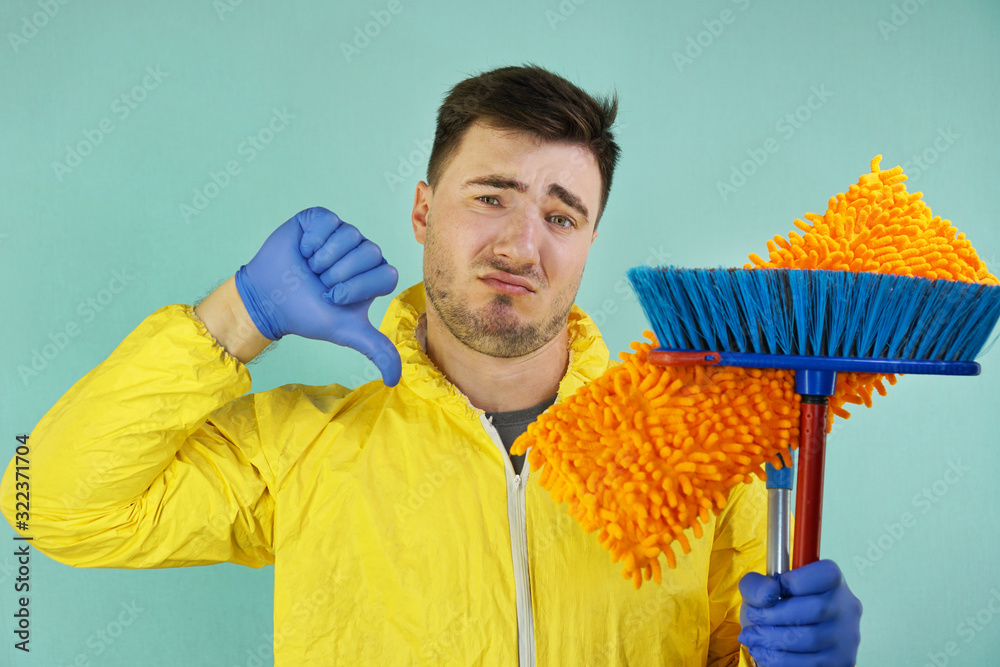Sad male cleaner with a mop and a broom in his hands in rubber stoves ...