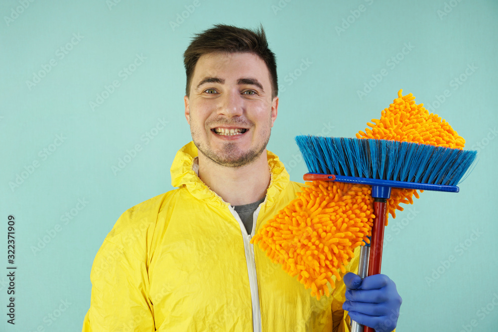 Cheerful male cleaner with a mop and a broom in his hands in rubber ...