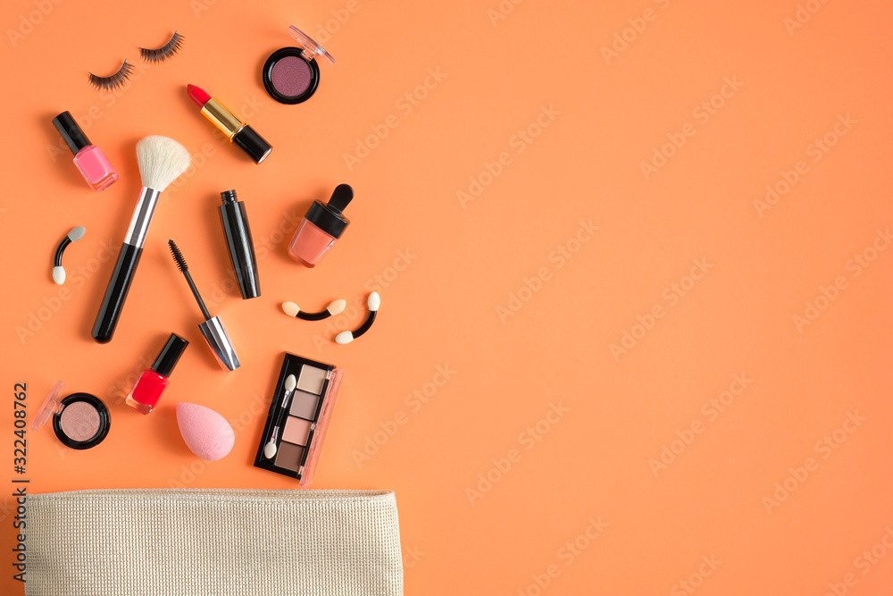 Makeup bag with cosmetic products spilling out on to a pastel orange ...