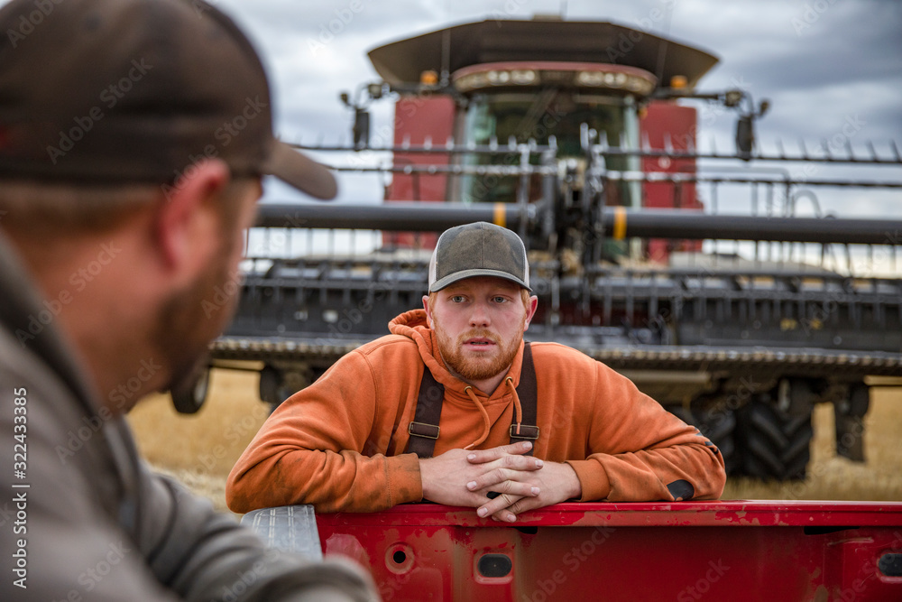 Male farmers talking at pickup truck in field with combine harvester ...