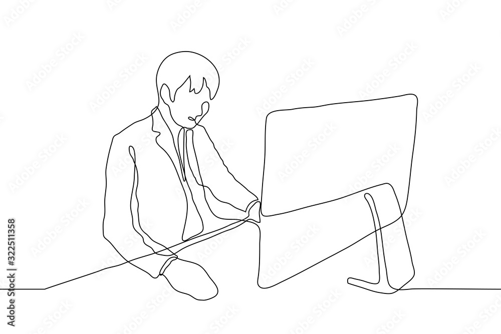 man in a suit sits at a desk looking at a computer screen and holding a ...