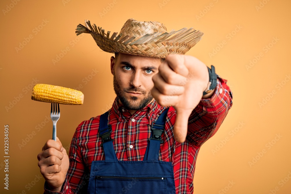 Young rural farmer man holding countryside corn over isolated yellow ...