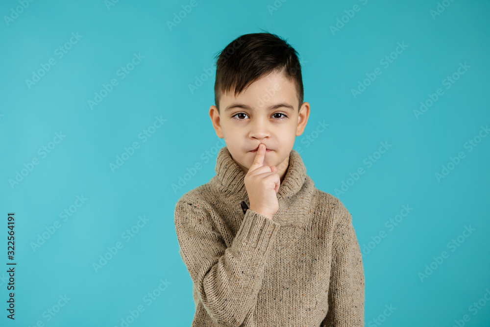 cute little boy asking to be quiet with finger on lips on blue ...