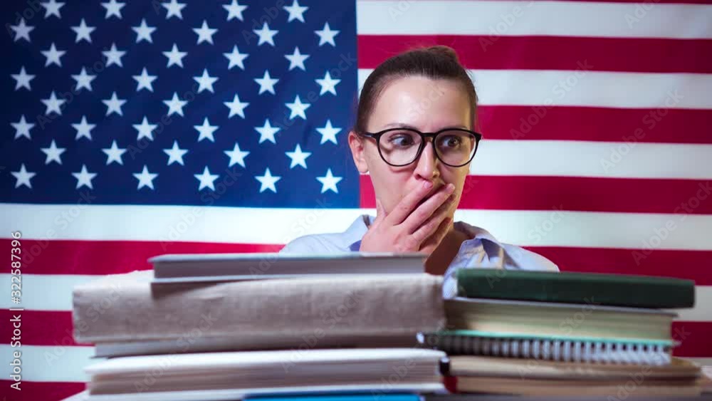 Student girl with glasses peeks out from under the stacks of books ...