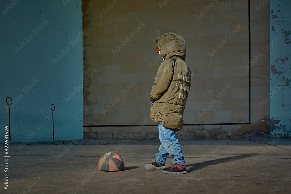 Boy with his hands in his pockets next to a deflated basketball ball ...