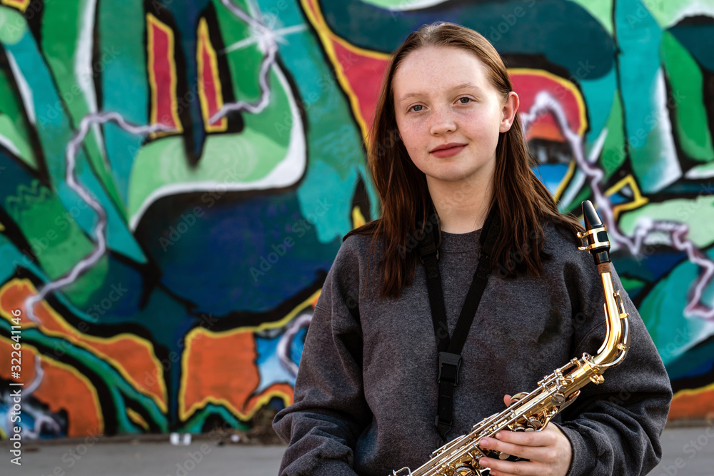 Female high school jazz musician posing with saxophone by graffiti ...
