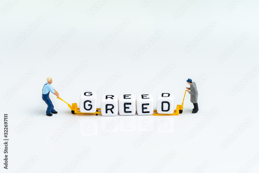 Miniature man pulling folklift with cube block building the word GREED ...