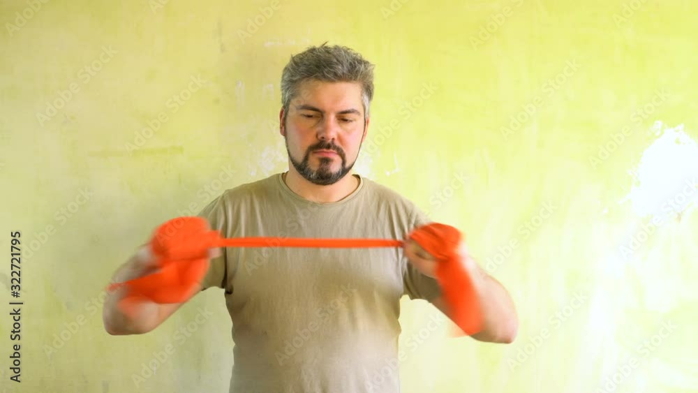 A bearded man is standing against the wall. In the hands of a rubber ...