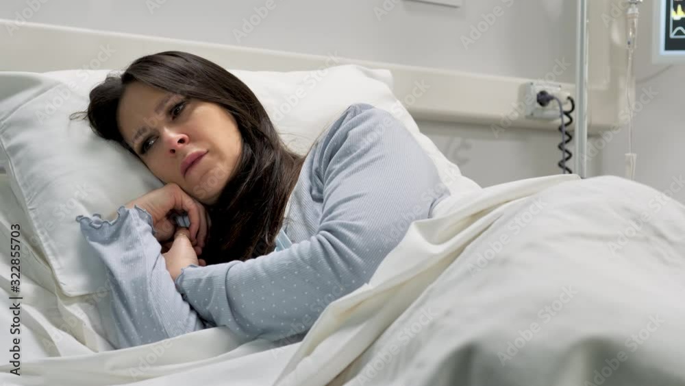 sad suffering female patient lying in the hospital bed staring into ...
