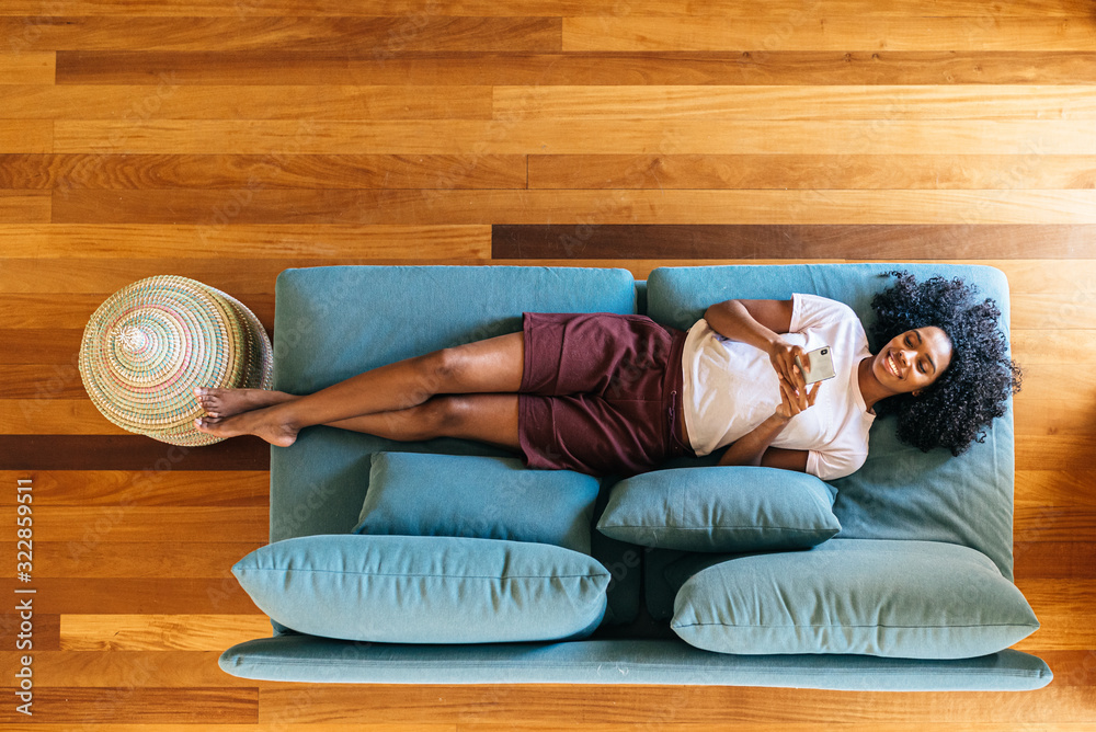 Black woman chatting on smartphone lying on couch at home Stock Photo ...
