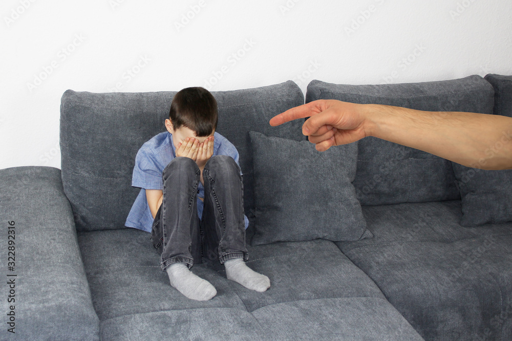 sad child, a boy sitting on a gray sofa in the room and covered his ...