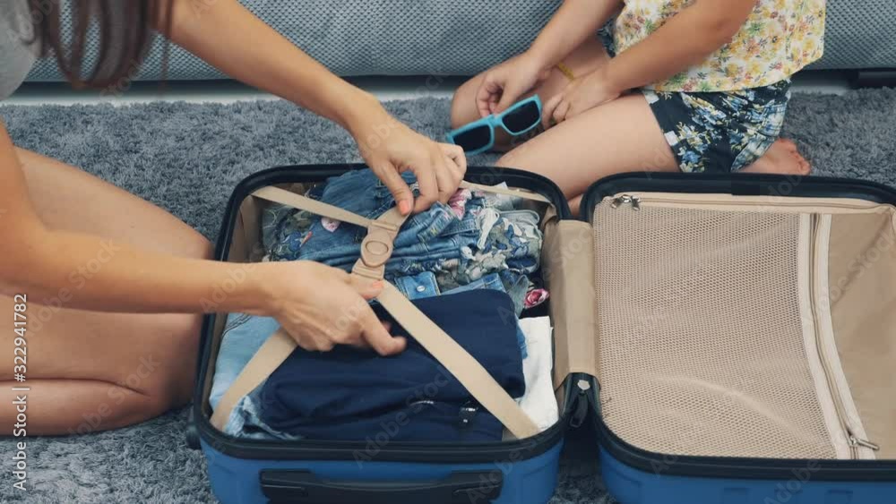 Mom is packing a huge blue suitcase. Little girl is hepling her ...