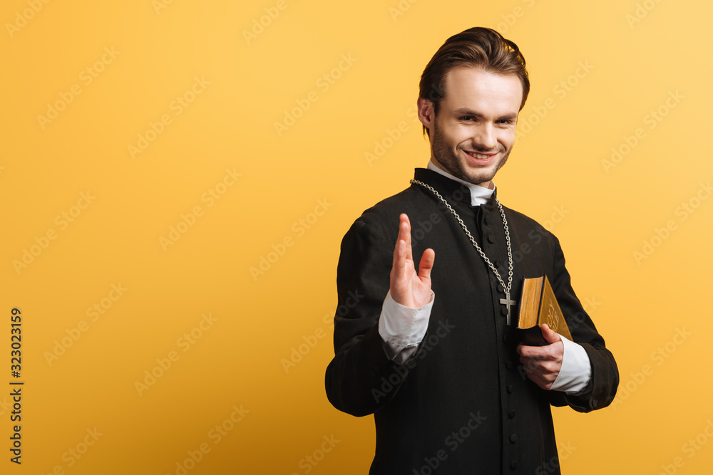 smiling catholic priest showing blessing gesture while holding bible ...