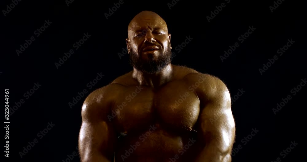 a large, bald, muscular man with a beard and bronze skin poses on a ...
