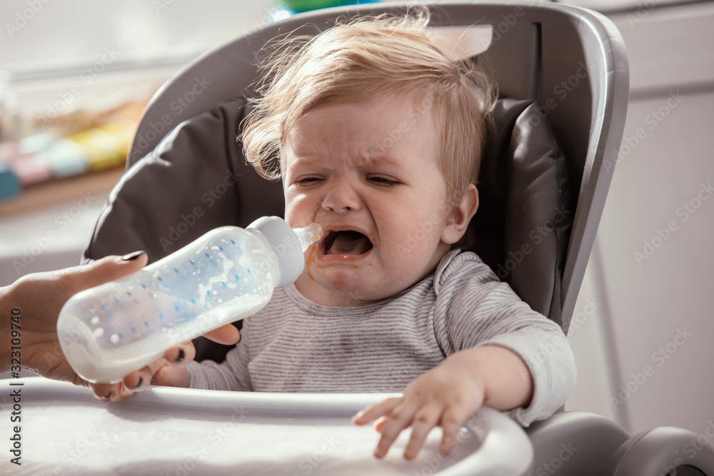 Beautiful baby in the child dining chair eat healthy food. Crying baby ...
