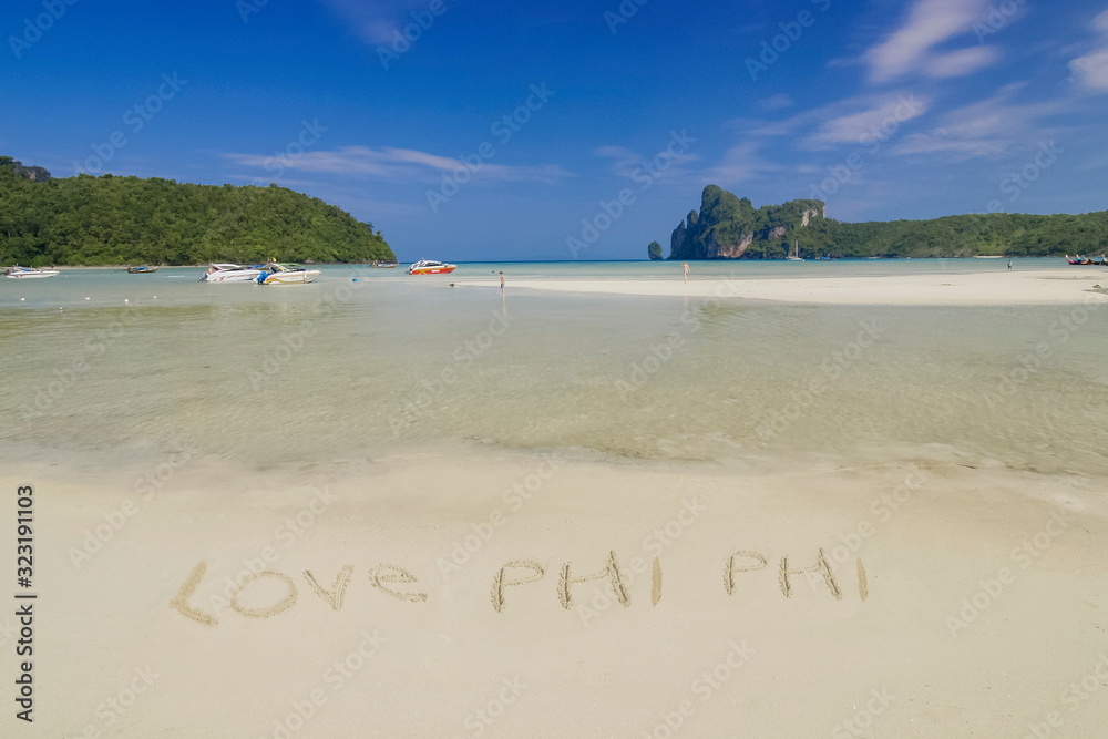 view of Love Phi Phi Text on white sand beach with blurred mountains and blue sky background ...