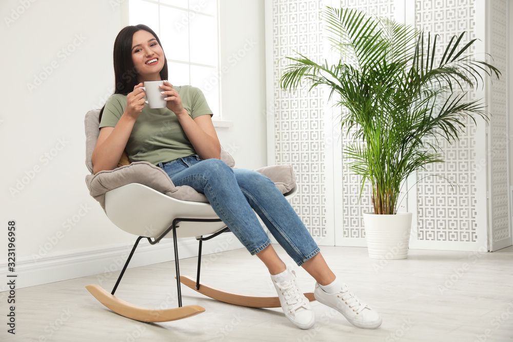 Young woman with cup of drink relaxing in rocking chair at home 素材庫相片 ...