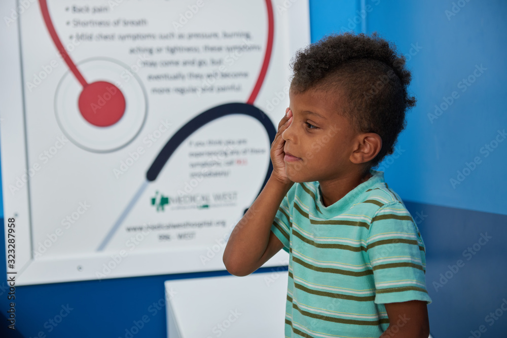 Little boy covering one eye with hand. Doctor ophthalmologist checks ...