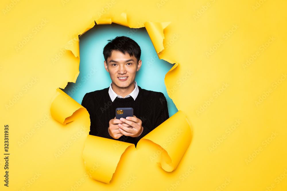 Foto de Young chinese man hold mobile phone keeps head in hole of torn ...