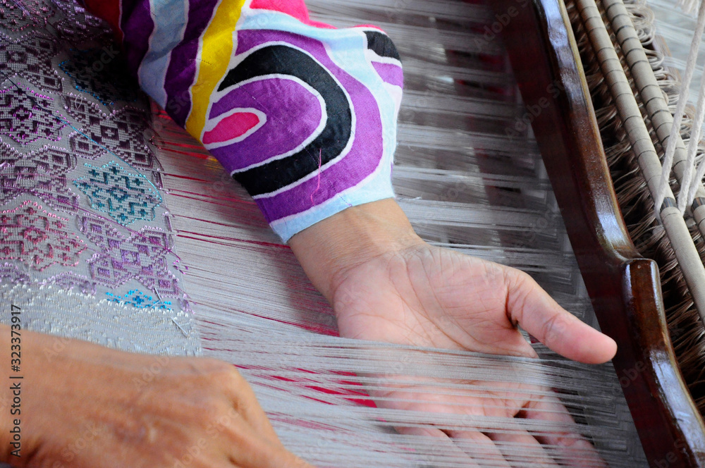 A woman is using traditional weaving machines to weave songket. Songket ...