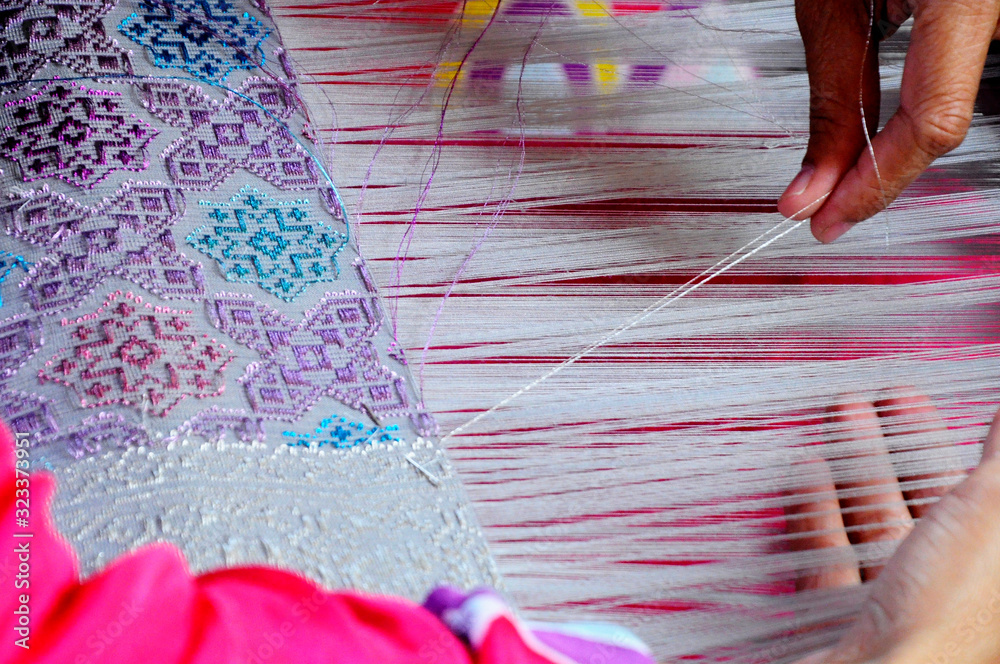 A woman is using traditional weaving machines to weave songket. Songket ...