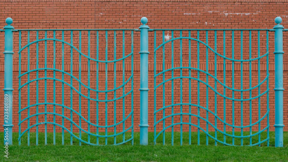 Aqua blue wavy fence built on grassed area with red brick wall behind ...