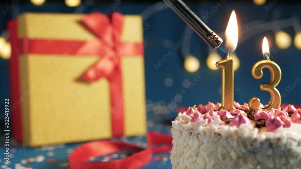 White birthday cake number 13 golden candles burning by lighter, blue ...