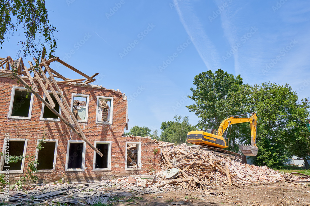 Destroyed old house and a yellow excavator on the wreckage. Demolition ...