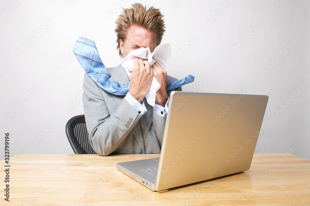 Allergic office worker sneezing in front of his laptop computer indoors ...