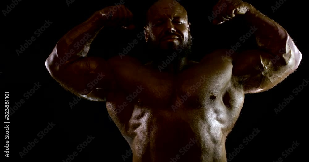 a large bald man with a beard and bronze skin poses on a black ...