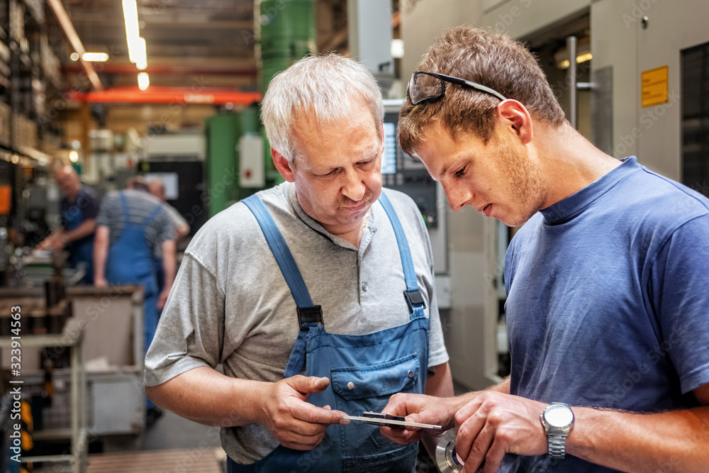 Skilled workers standing in a production hall in front of a machine ...