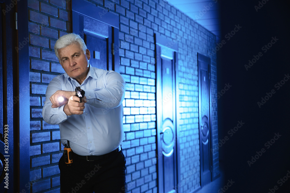 Professional security guard with gun and flashlight checking dark ...