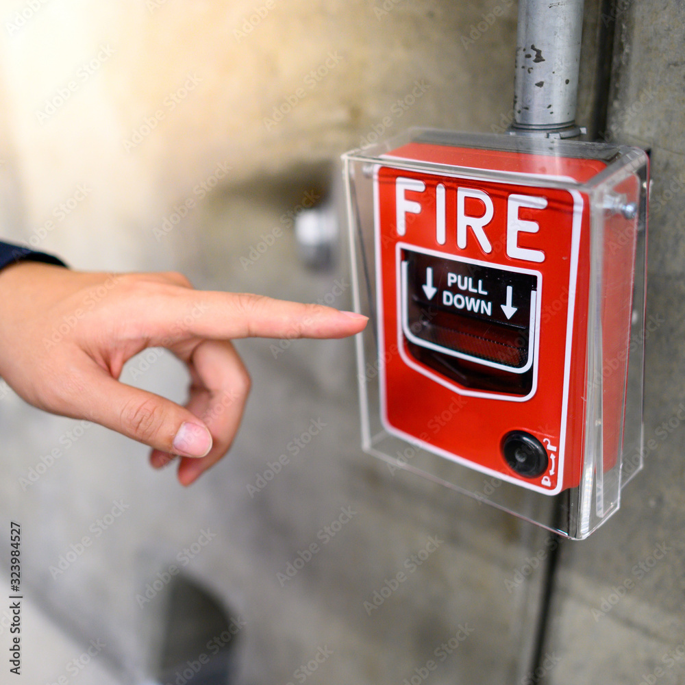 Male hand pointing at red fire alarm switch on concrete wall in office ...