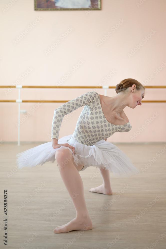 A very flexible ballerina in a tutu stands in a plie in a class with ...