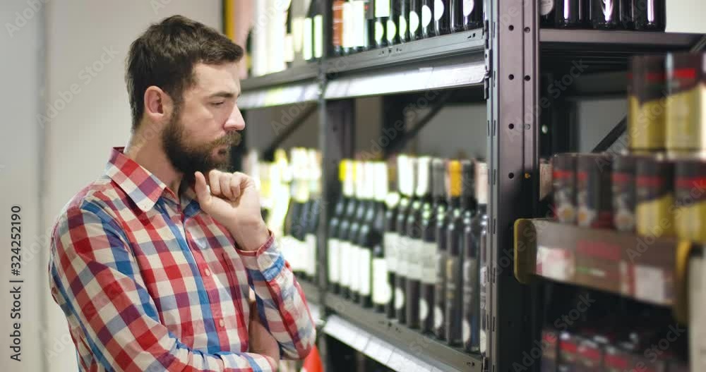 Side view of thoughtful bearded Caucasian man looking at shelves with ...