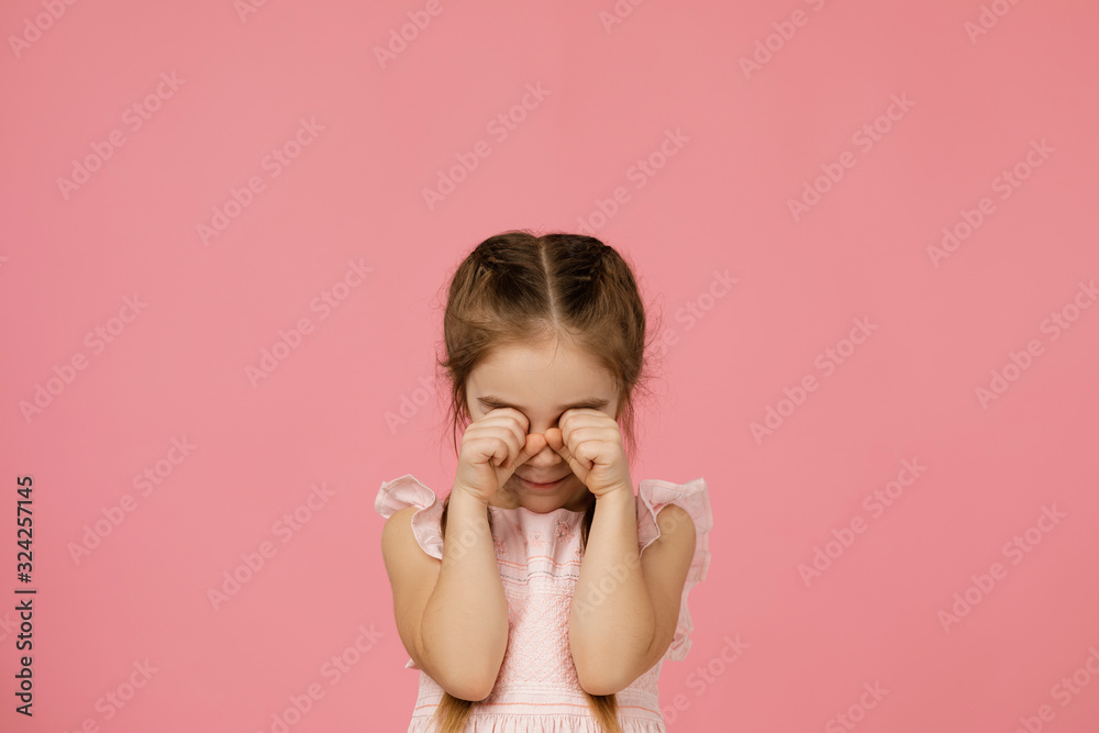 upset little child girl is crying on pink background. girl wiping tears ...