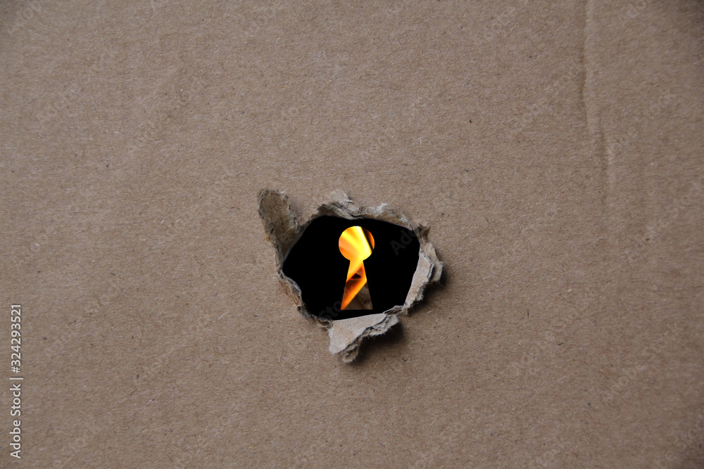 black keyhole with bright yellow fire in a torn hole of gray rough ...