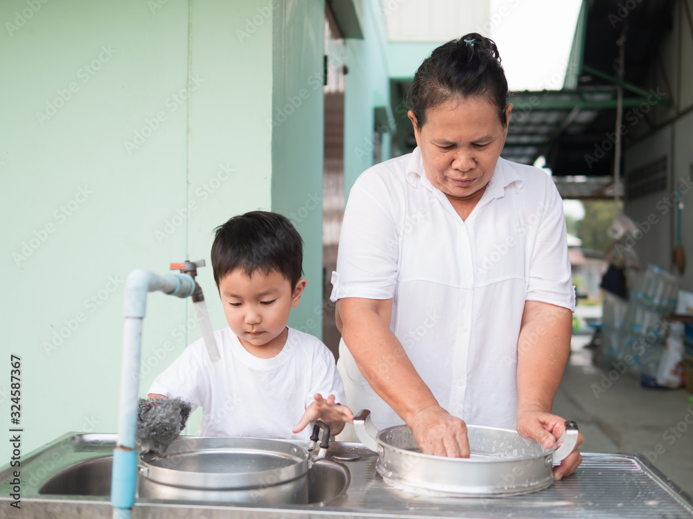 Asian little child boy helping grandmother wash pot with happy smiling ...