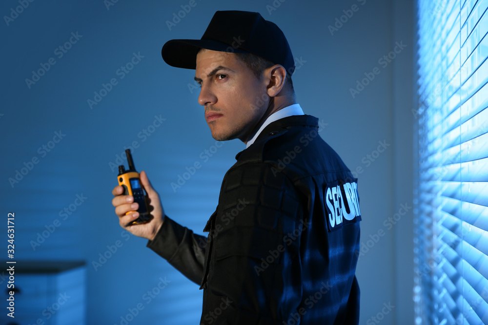 Professional security guard with portable radio set near window in dark ...