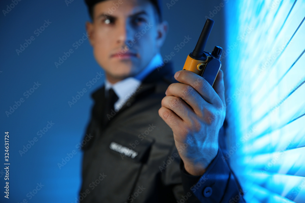 Professional security guard with portable radio set near window in dark ...