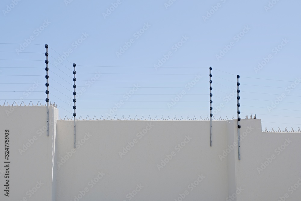 long upright poles holding electric fencing cable on a boundary wall ...