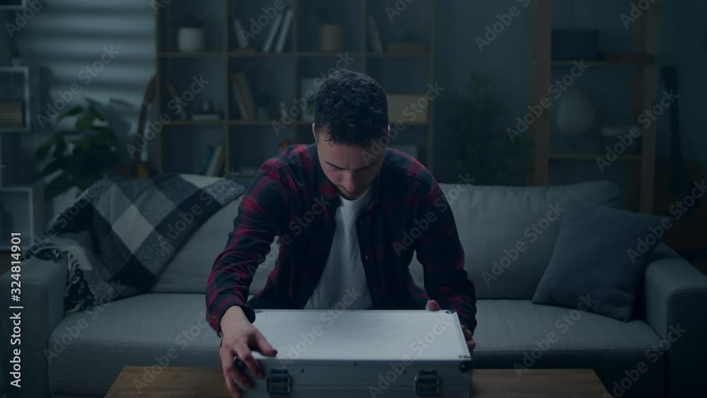 A young man opens a case at home at night. From which a bright golden ...