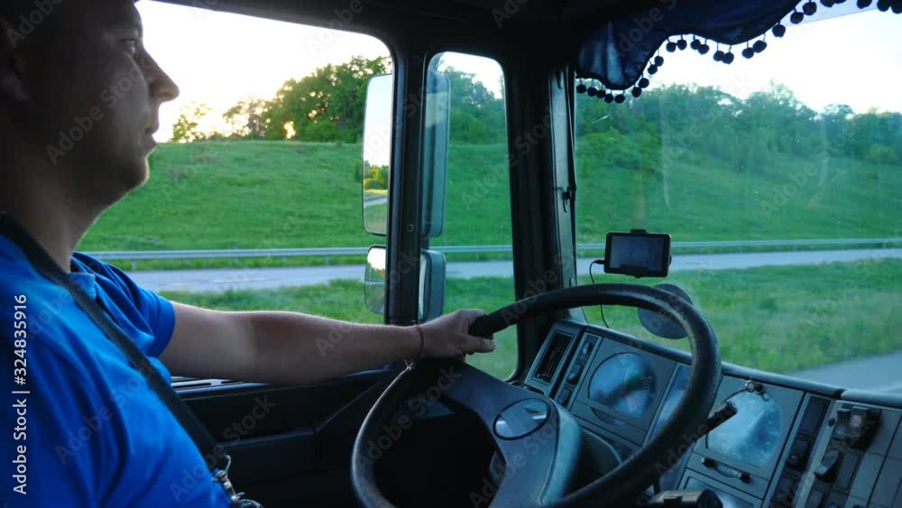 Lorry driver riding through countryside at sunset time. Man controlling ...