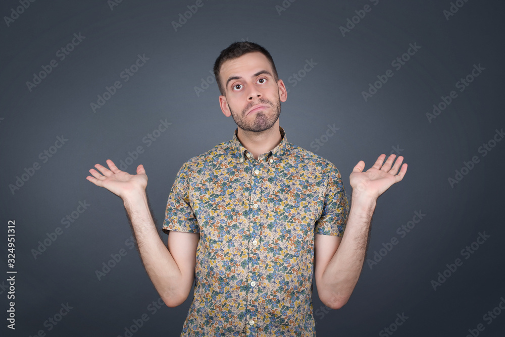 Puzzled and clueless young man with arms out, shrugging his shoulders ...