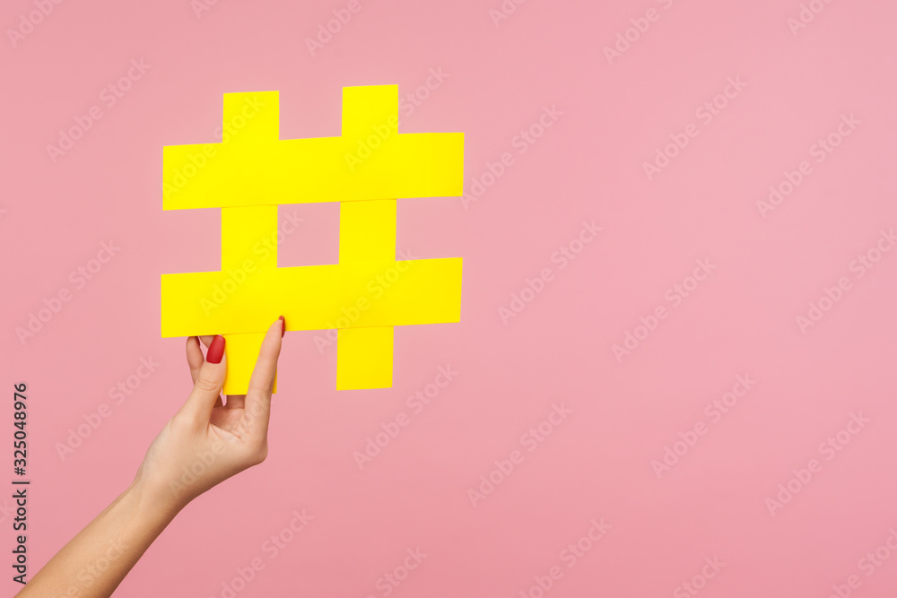 Closeup of hand holding large yellow paper hashtag symbol next to copy ...