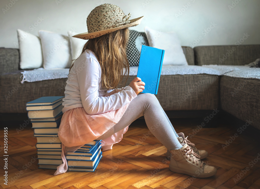Little girl reading book. Girl with a pile of books at home. Having fun ...
