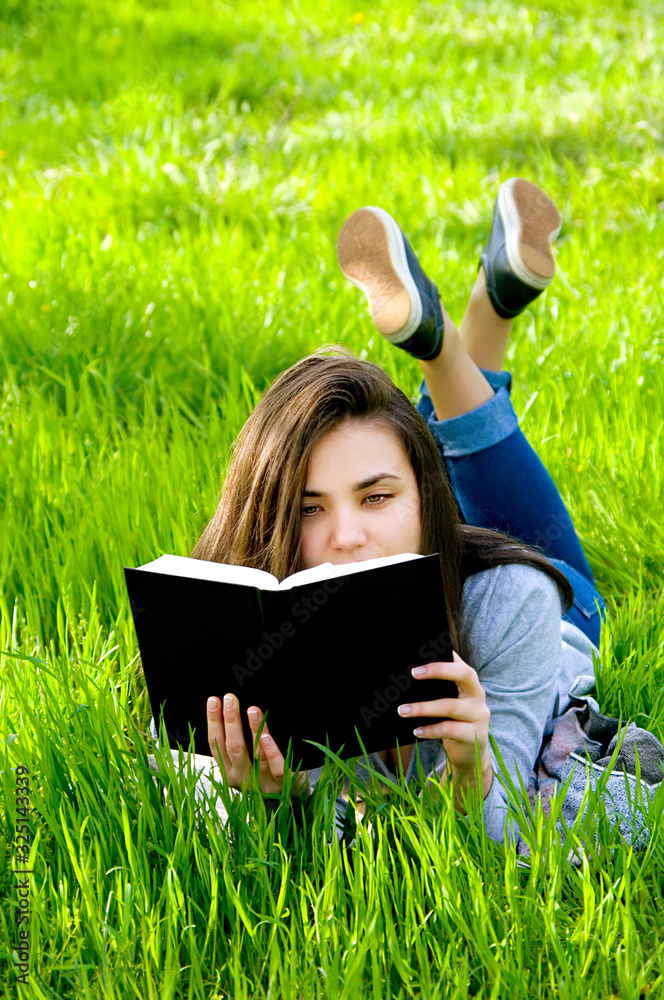 beautiful young woman girl reading a book in a park lying on the grass ...