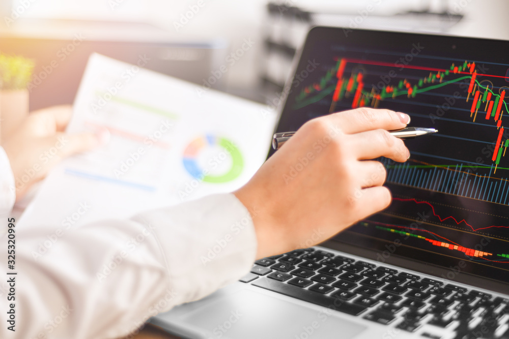 Business woman shows at graph on laptop and writing into notes or ...