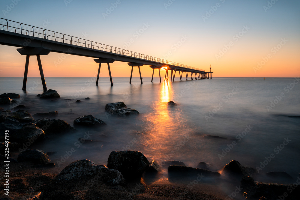 View of a sea dock at dawn from the beach with long exposure creating a ...