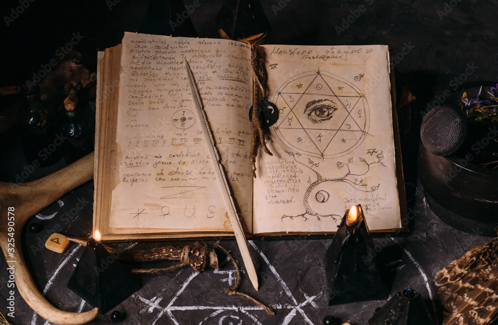 Open old book with magic spells, runes, black candles on witch table ...